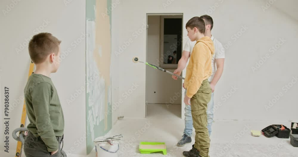 Father and his son painting a wall with yellow paint in a room of their ...