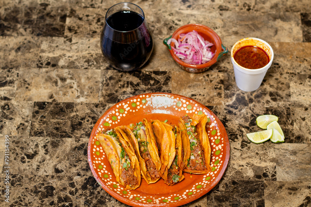 high view of four birria tacos on a clay plate with consome, onion, and ...