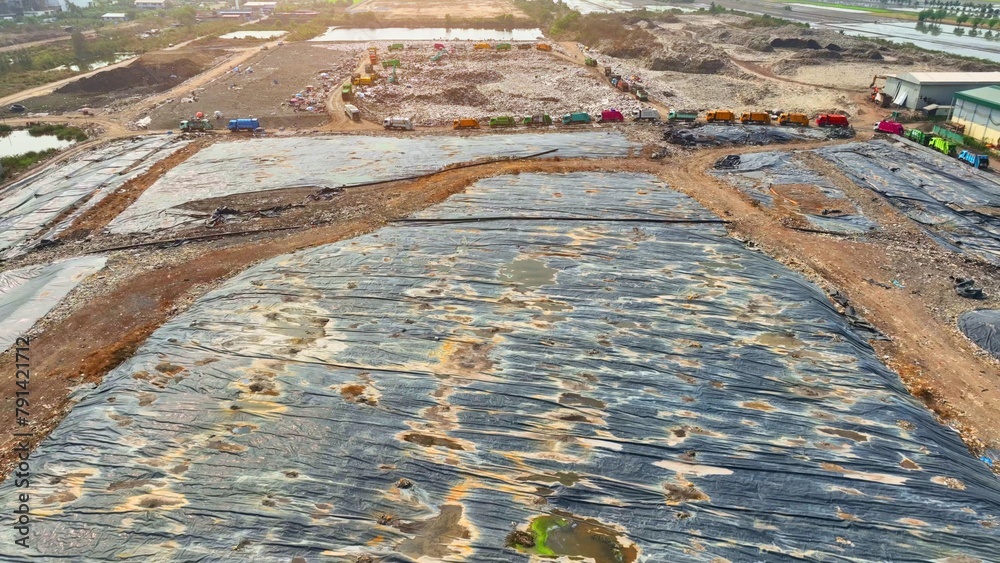 A sprawling landfill concealed under expansive black plastic sheets, a ...