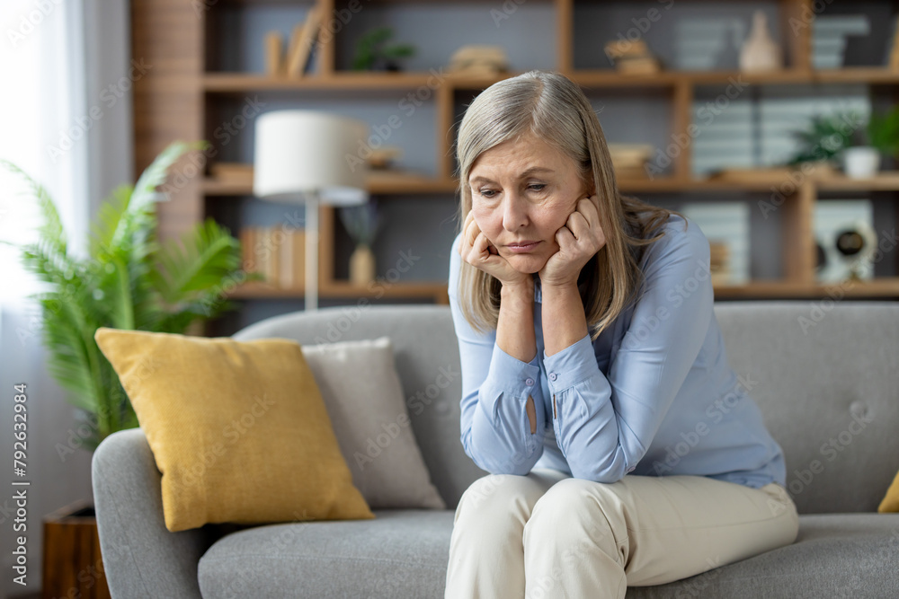 A mature woman appears contemplative and sad as she sits alone on her ...
