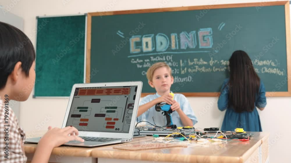 Asian boy coding program while caucasian friend fixing electric board ...