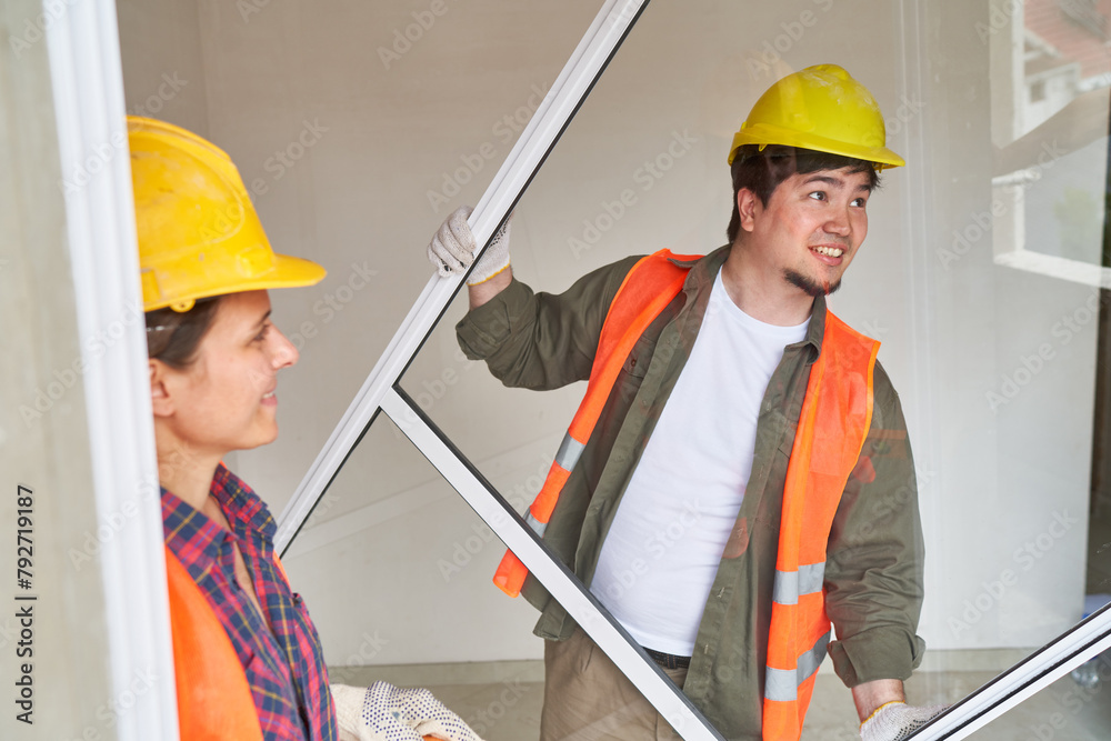 Smiling male carpenter carrying window frame by female coworker at ...