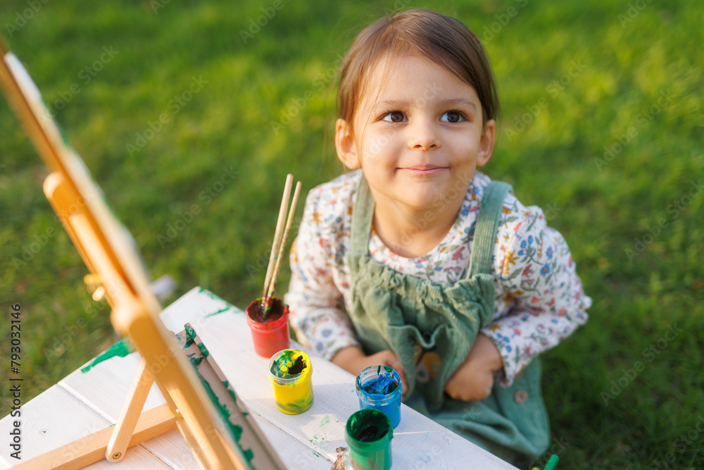 Little girl is painting a picture in the park on the green grass. Child ...