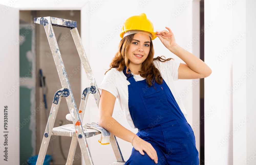 Positive young female builder wearing blue workwear with yellow safety ...