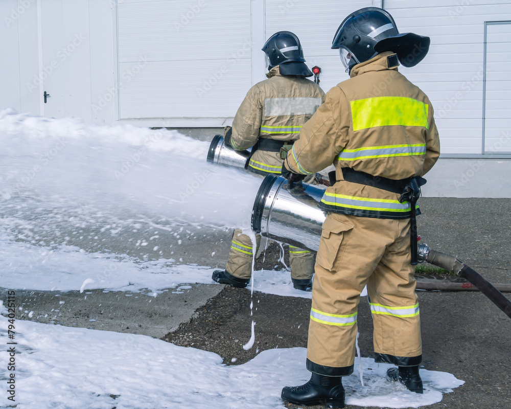 Firefighters in protective clothing use a foam generator to supply foam ...