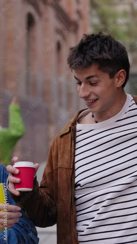 Vertical happy students strolling around the university campus with workbooks and drinking ...