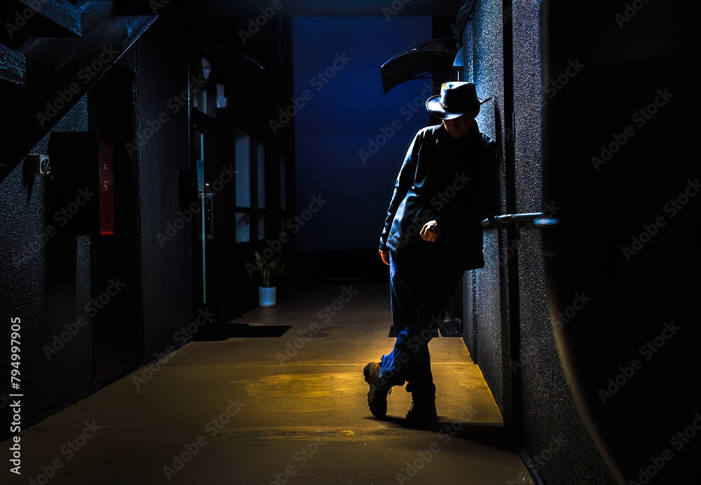 Silhouette of a man leaning against a wall in a dark alleyway at night ...