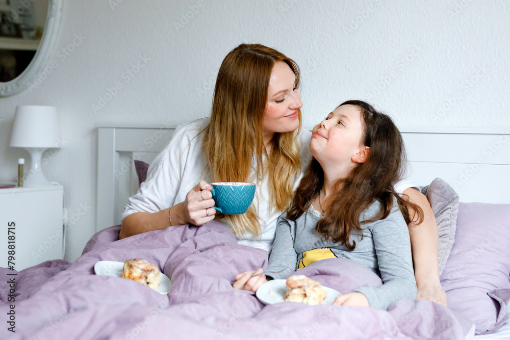 Lovely young mother and cute school kid girl cuddling together in bed ...