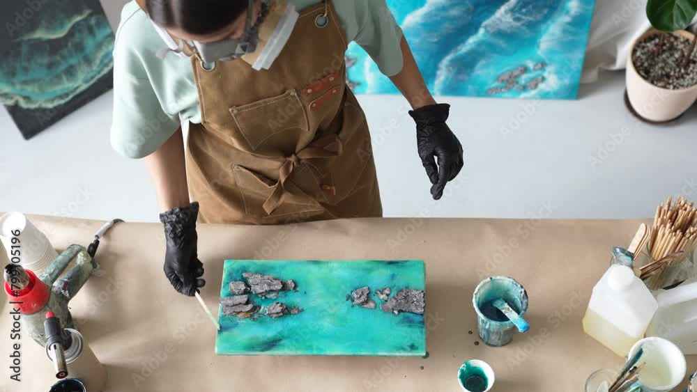 Woman artist pours epoxy resin and smears it with stick on wooden board ...