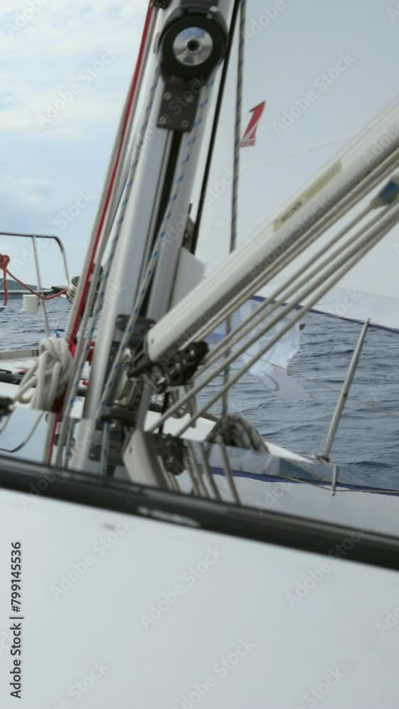 A sailboat is in the water with a white sail. The sail is attached to a ...