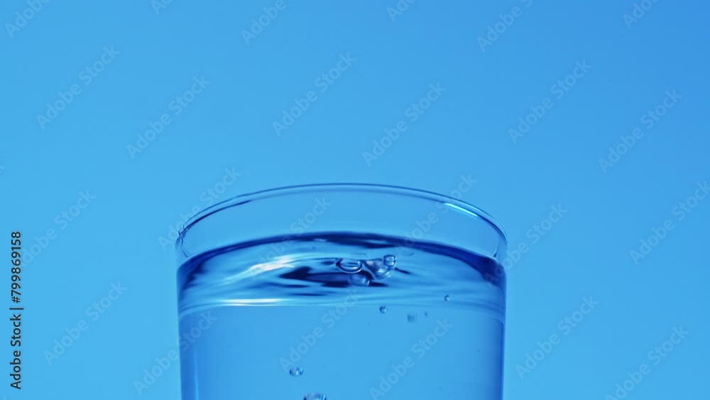 Close-up of Pill falling down in a glass of water. Effervescent tablet ...