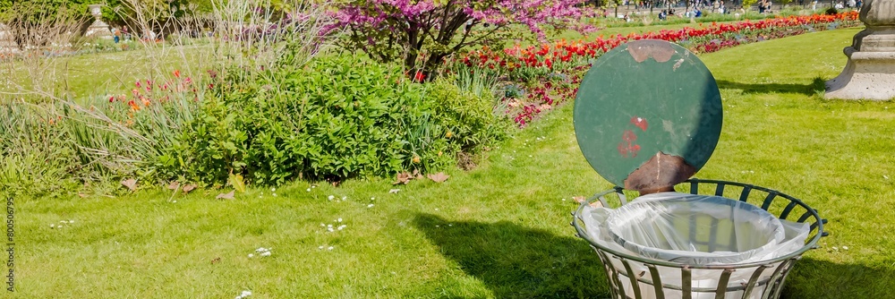 Vibrant public park in spring with overflowing trash can, highlighting ...