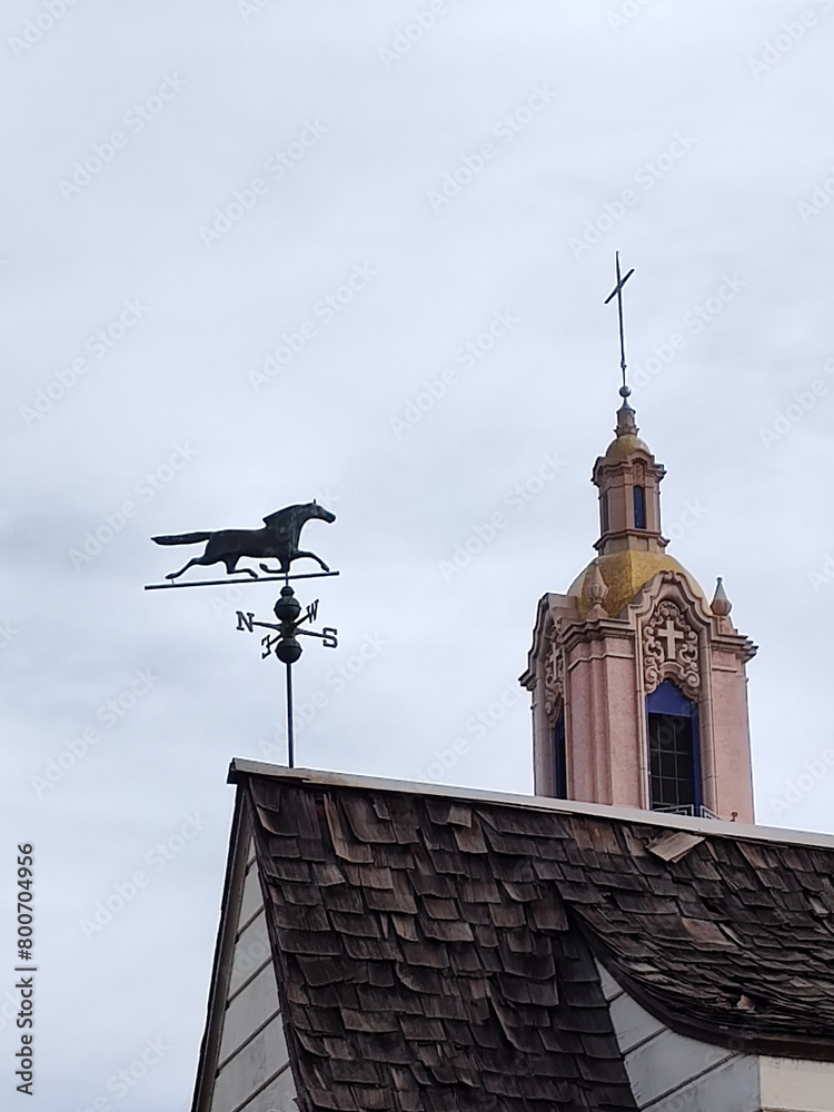View of an old town shingle roof with a horse shape vane and a church ...