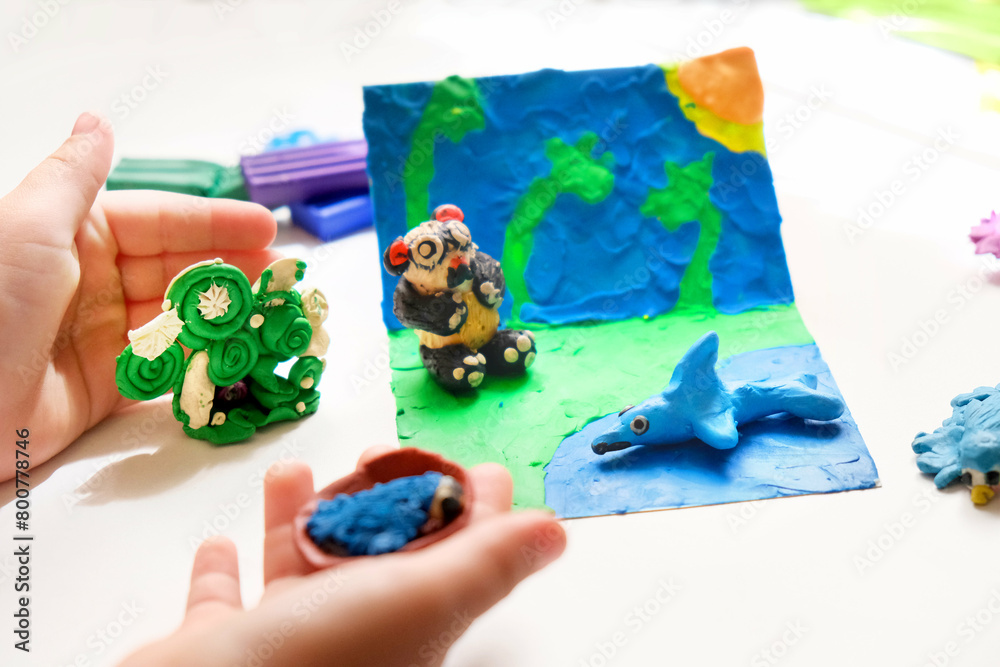 Child smearing colorful plasticine on cardboard and creating fairy tale ...