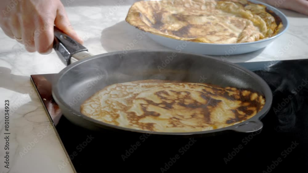 Close-up video, a thin pancake is being cooked in a pan, the cook moves ...