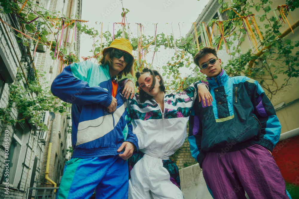 Three young people, friends wearing 90s inspired sportswear, colorful ...