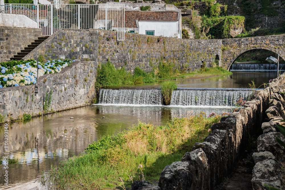 Blurred wall next to stream flowing in weirs and old stone bridge in ...