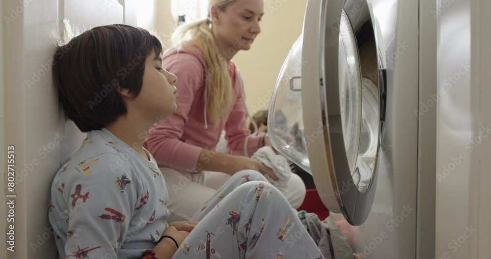 A mother supervises her young kids, dressed in pajamas, as they watch ...