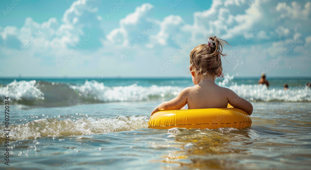 Cute little girl in a swimming ring on the beach, sitting and relaxing ...