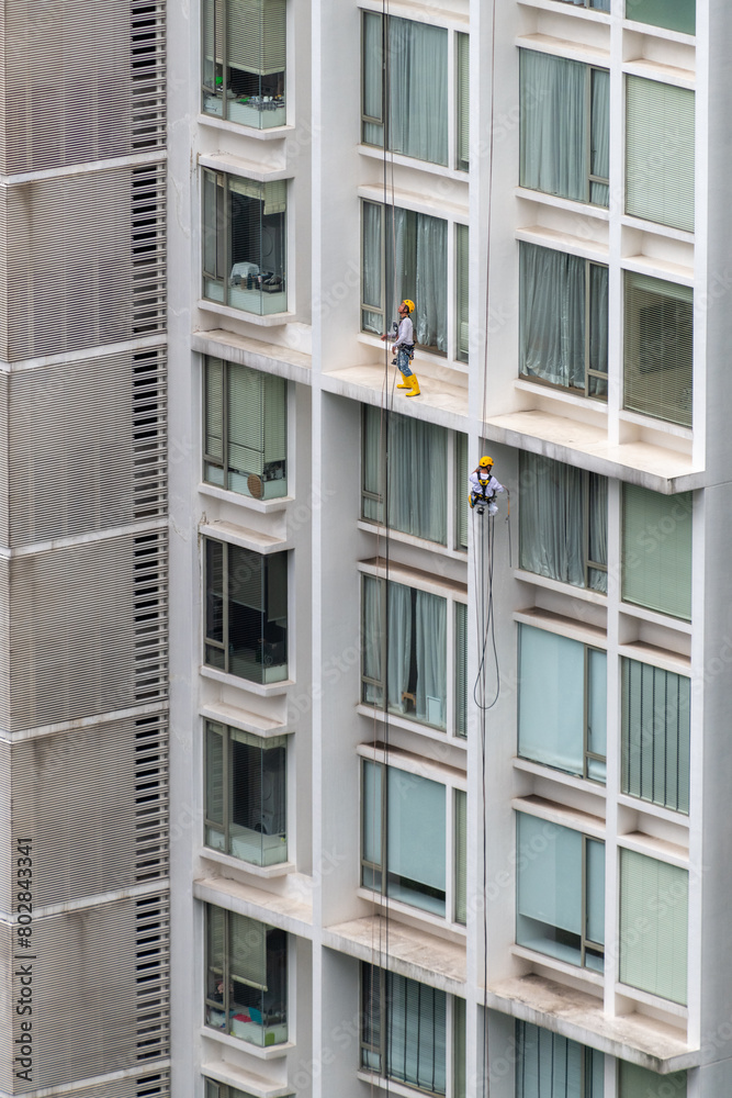 Two men working at height in a high-rise condo in Asia wearing safety ...