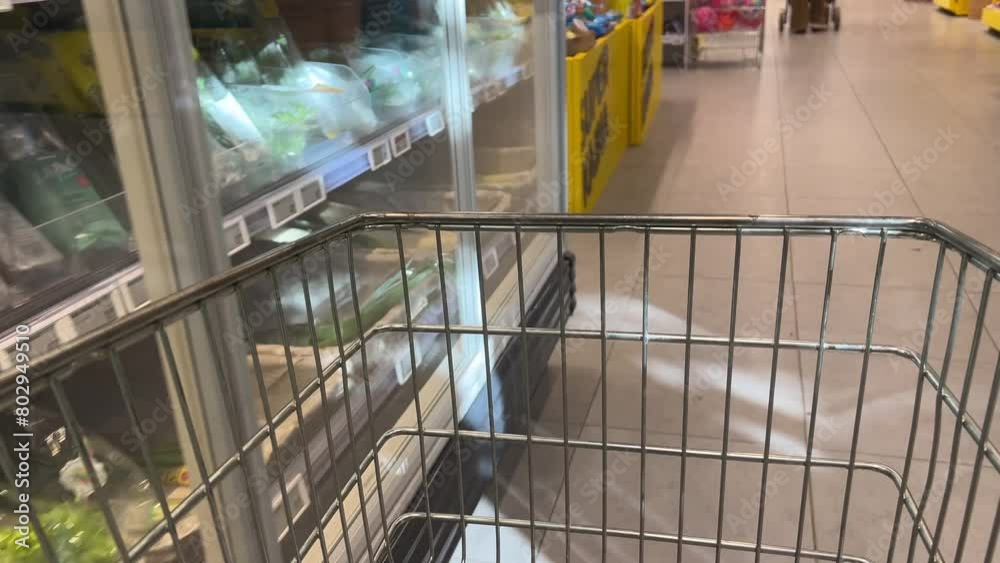 An empty grocery cart rides between food counters in a grocery store ...