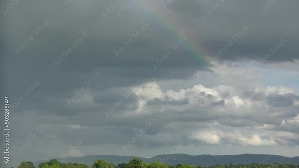 Moving dark grey rainy clouds and colorful rainbow over horizon of ...