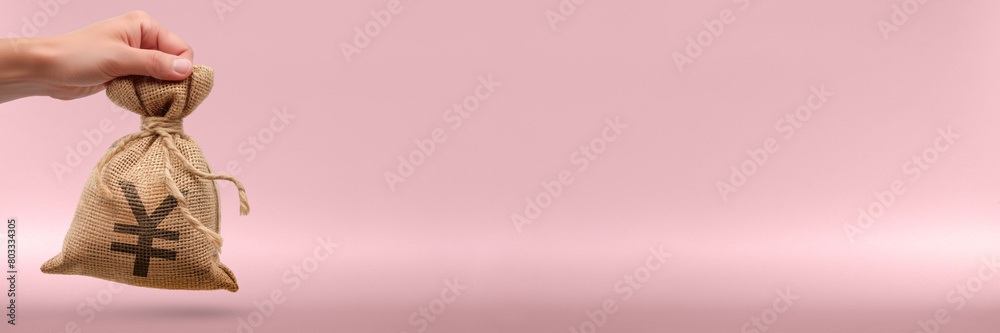 Hand holding a money bag with the Japanese yen symbol on a pink ...