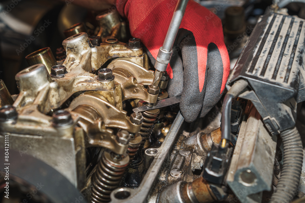 The mechanic is adjusting the valve clearance on a car engine. Auto ...