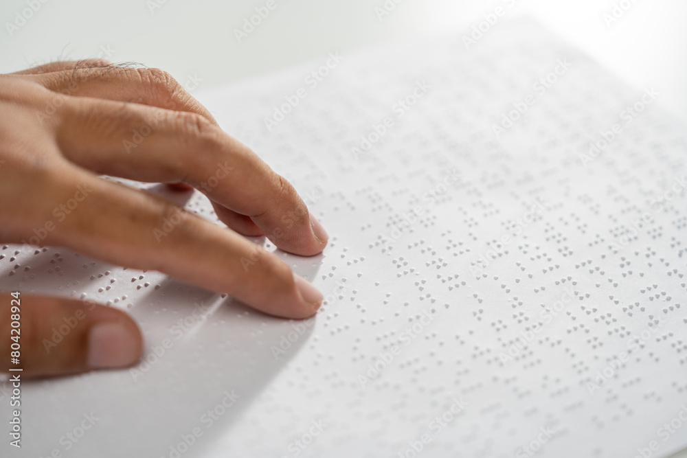Hand of a blind person reading some braille text on page paper to learn ...