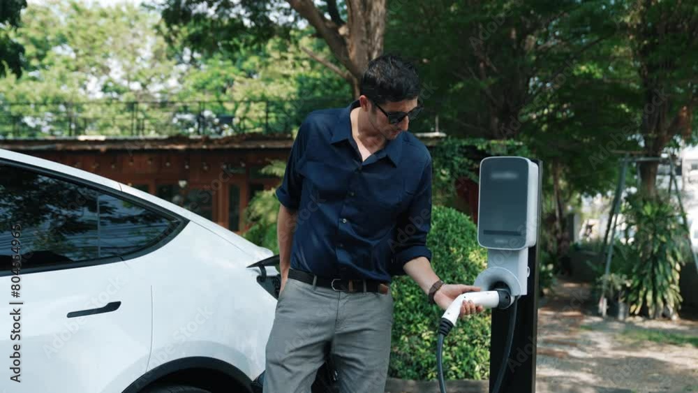 Young man and sustainable urban commute with EV electric car recharging ...