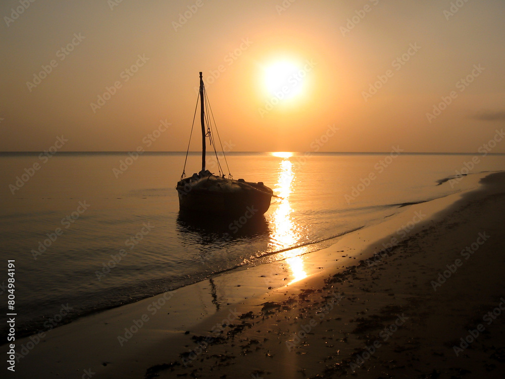 Silhouette of a Dhow at sunset, giving everything a golden color, in ...