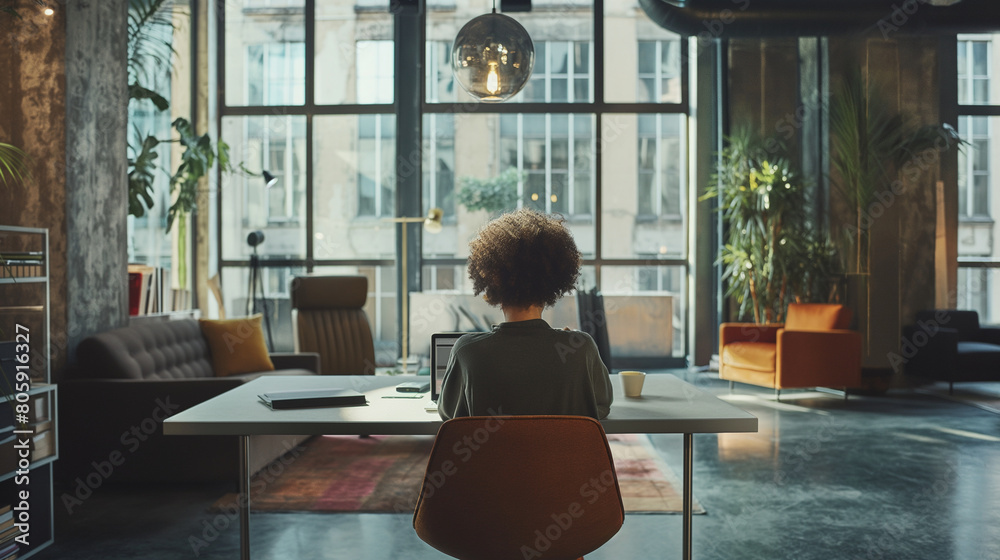 In a corporate office setting, a person sits at a laptop with a blank ...