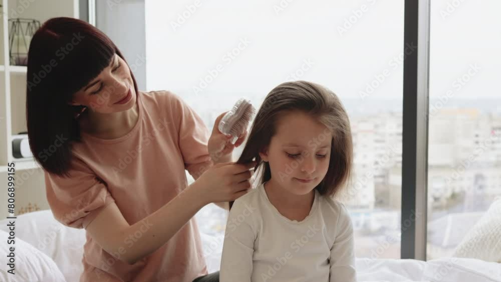Charming little girl smiling while her cheerful mom brushing daughter's ...