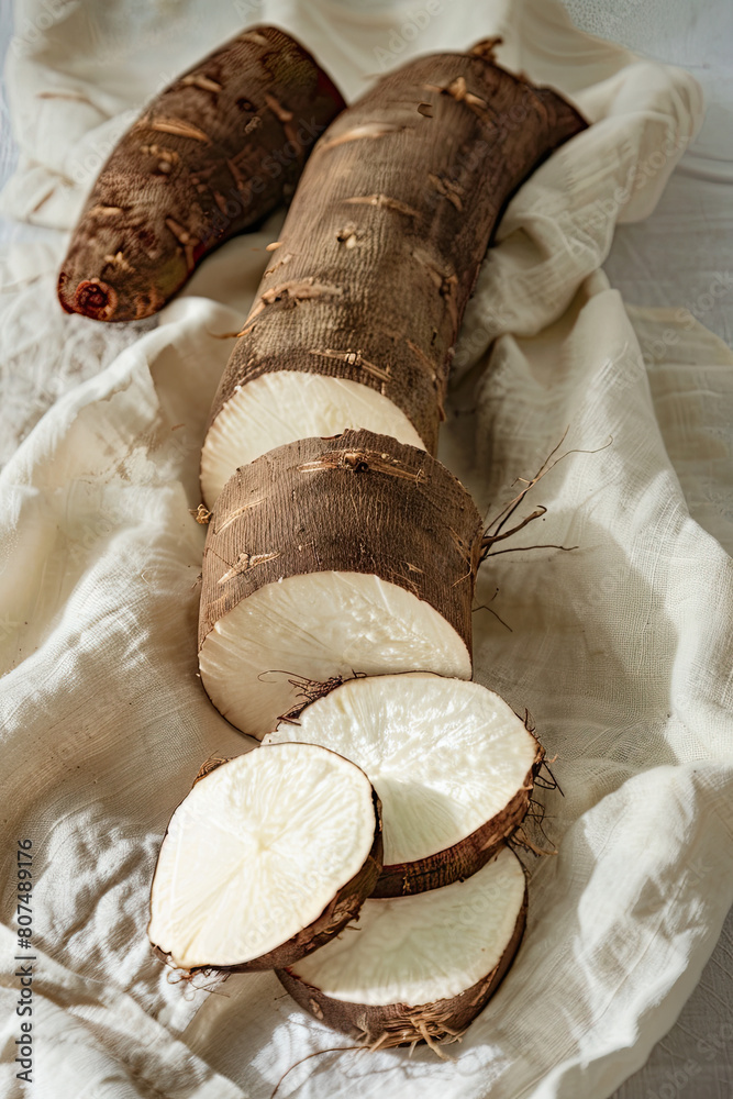 Rustic display of whole and sliced yuca root on light linen ...