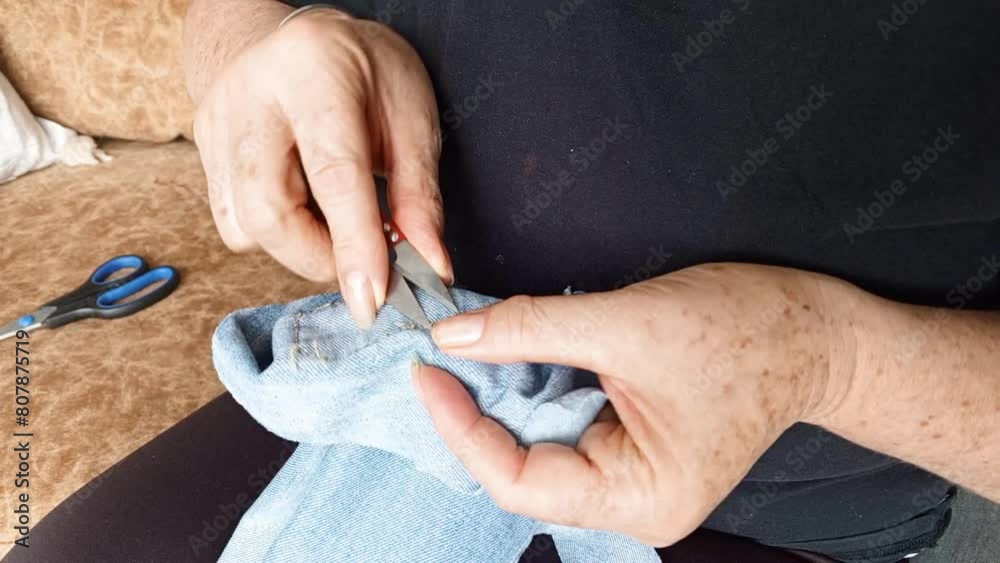Horizontal view of a woman's hands using sewing scissors to break the ...