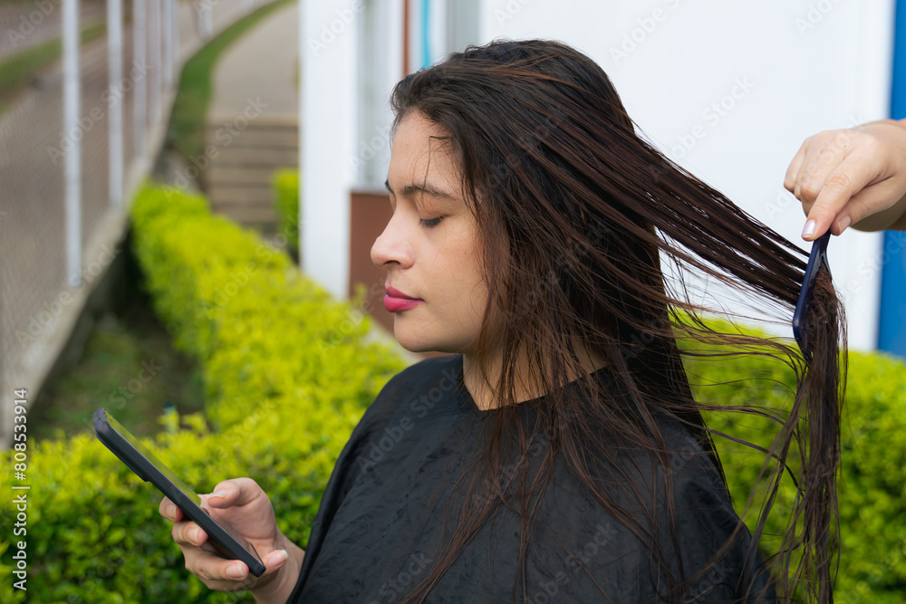 Latina mother stylist cutting her daughter's dark hair outdoors while ...