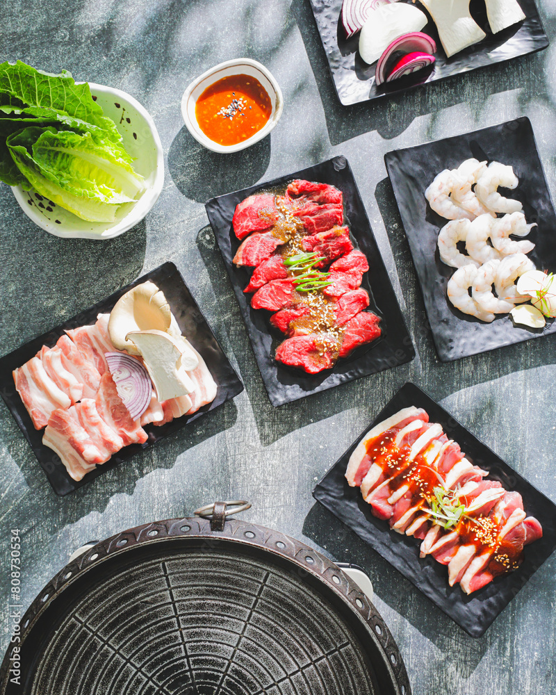 Top-down view of a Korean food barbecue setup with plates of raw beef ...