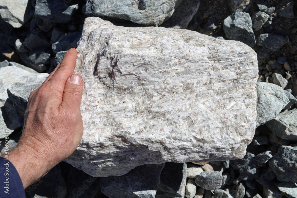 Hand, large pegmatite spodumene ore rock amongst waste (barren in ...