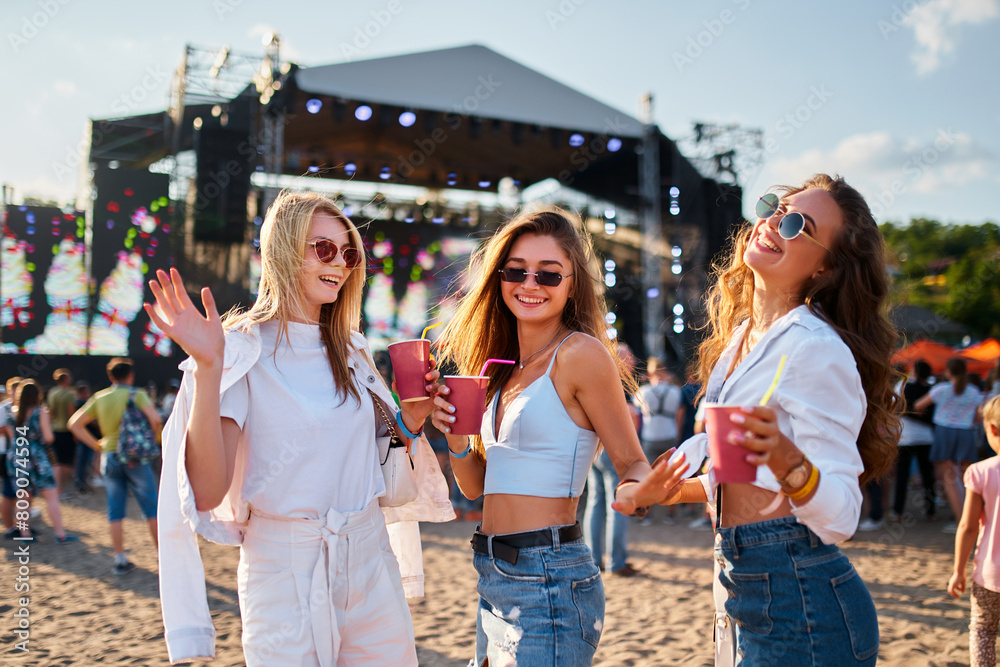 Girls enjoying summer music festival on beach, holding drinks, dancing ...