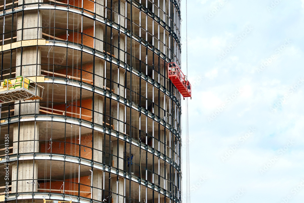 Workers on construction cradle prepare building for structural glazing ...