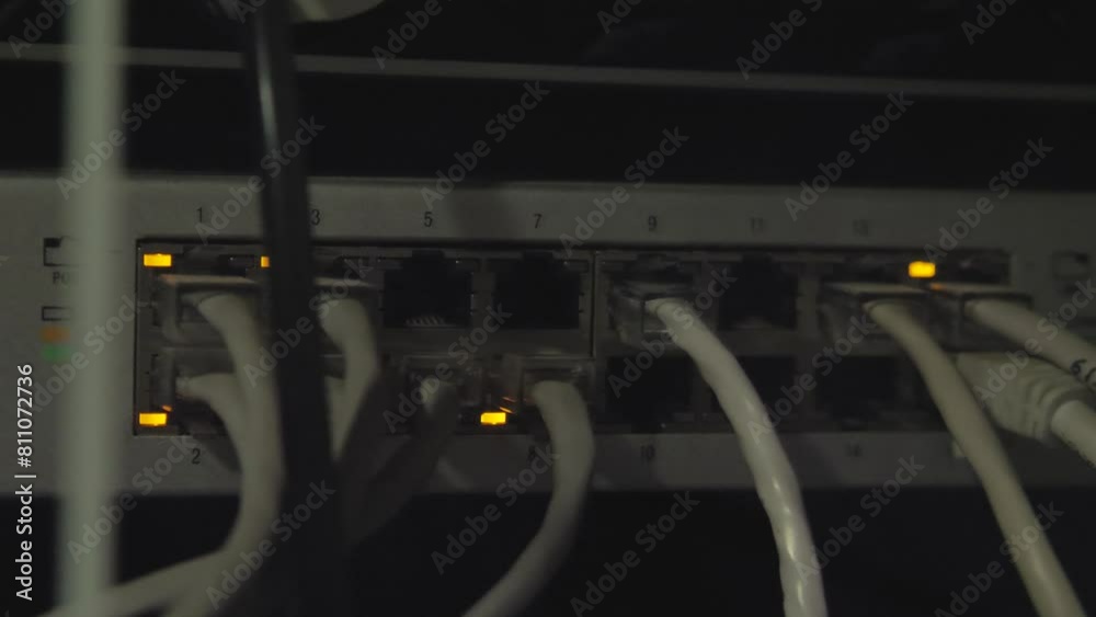 A rack-mounted network switch in a dimly lit room with Ethernet cables ...