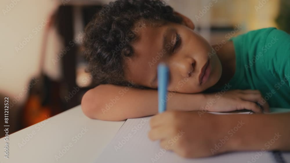 Tired schoolboy works on homework, writing in notebook, lack of ...
