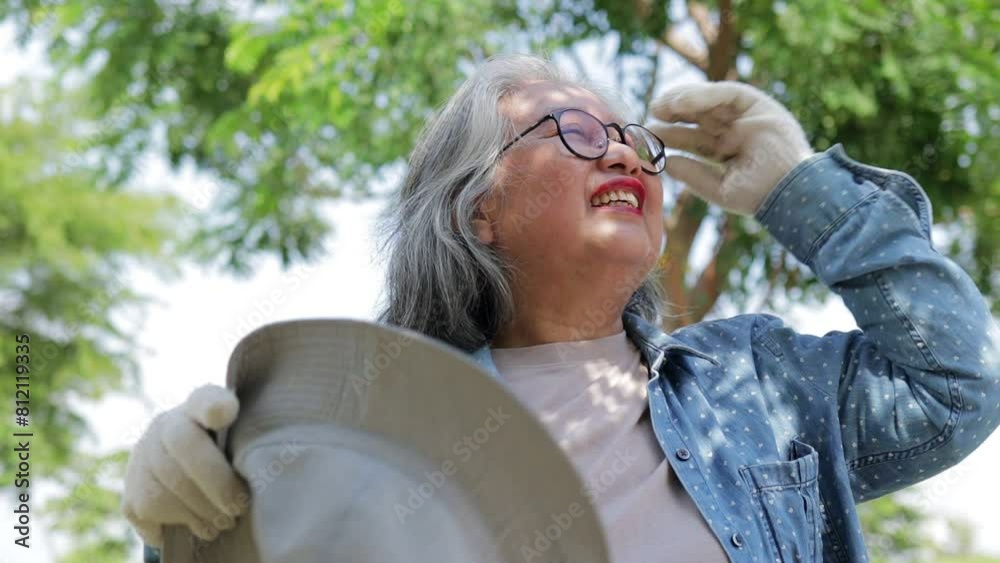 An elderly female farmer wearing glasses stands under a tree to avoid ...