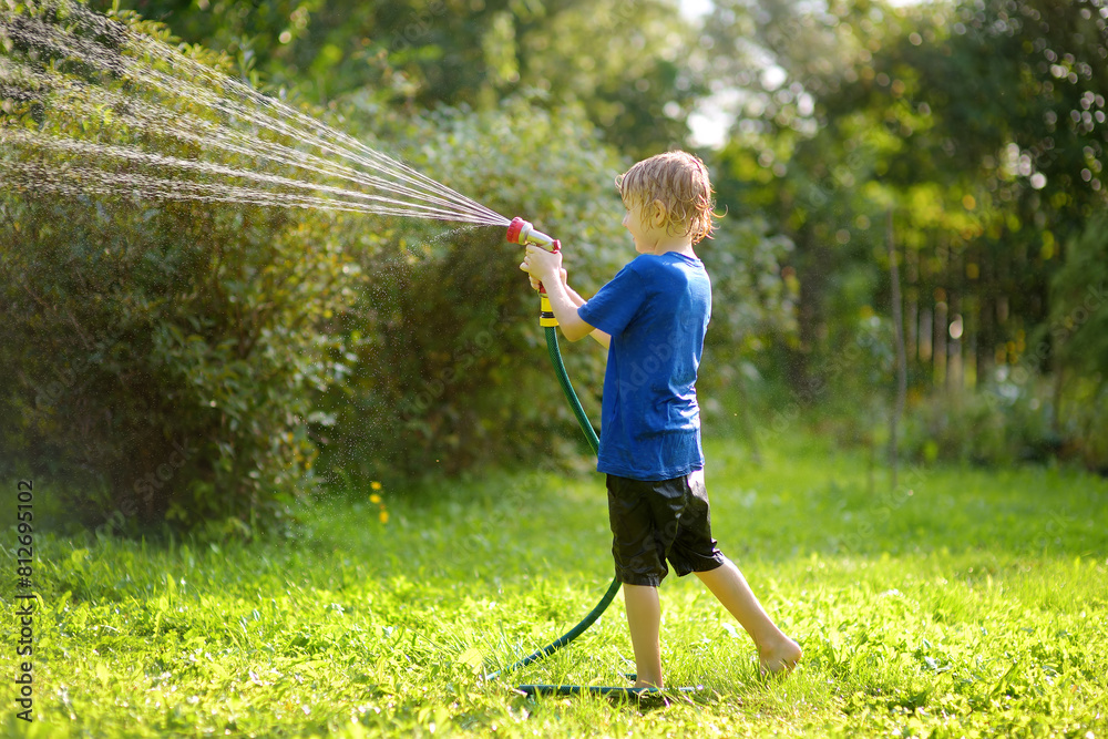 Funny little boy playing with garden hose in sunny backyard ...