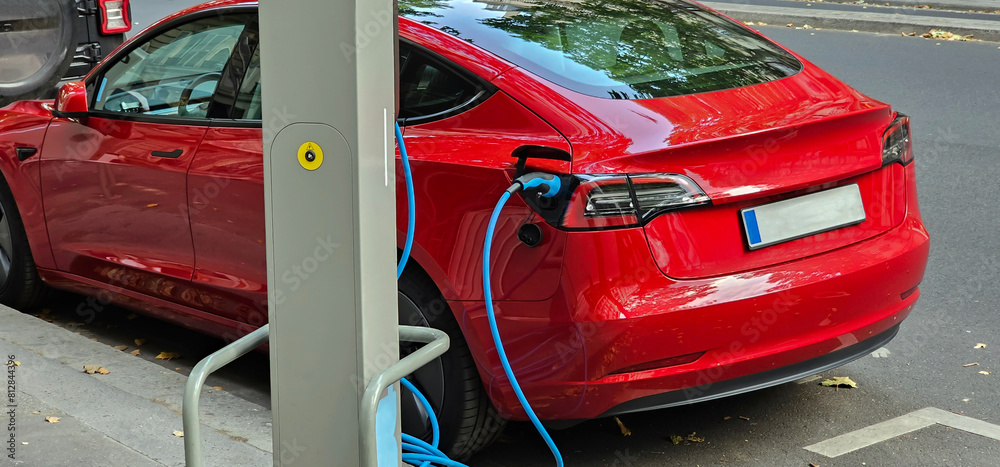 Red, shiny, modern electric vehicle, plugged into an on-street charging ...