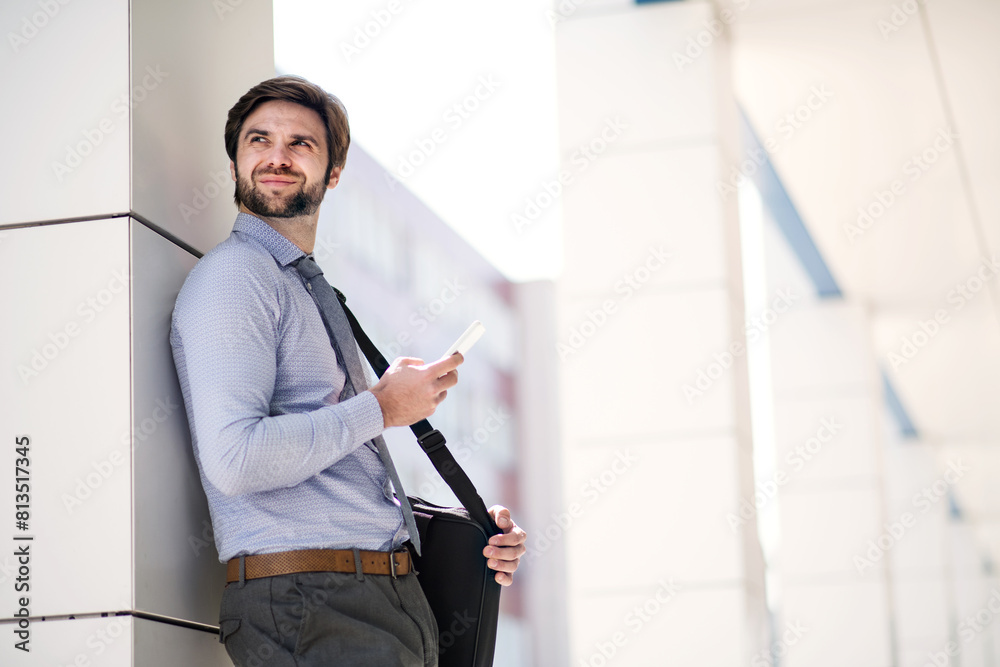 Handsome businessman scrolling on smartphone standing in front office building going to work ...
