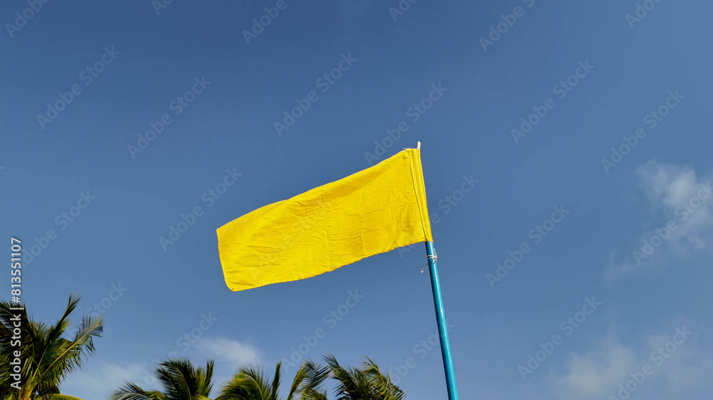 Bright yellow flag fluttering against a clear blue sky with tropical ...