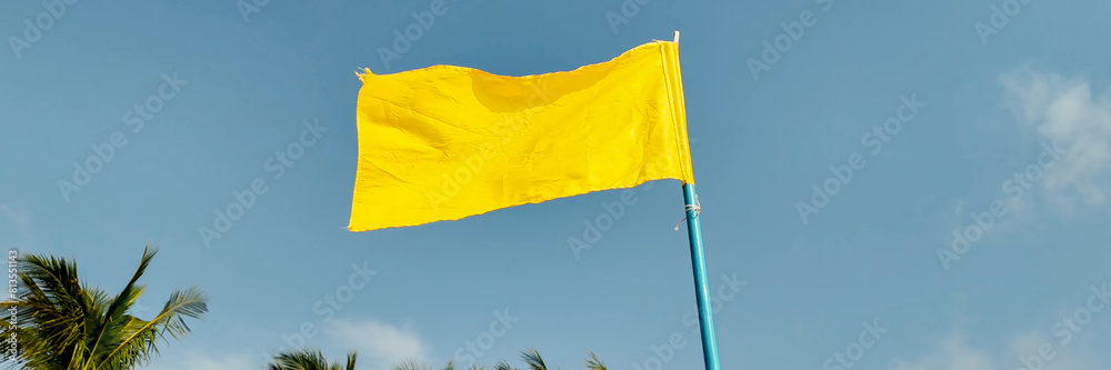 Bright yellow flag fluttering against a clear blue sky with tropical ...