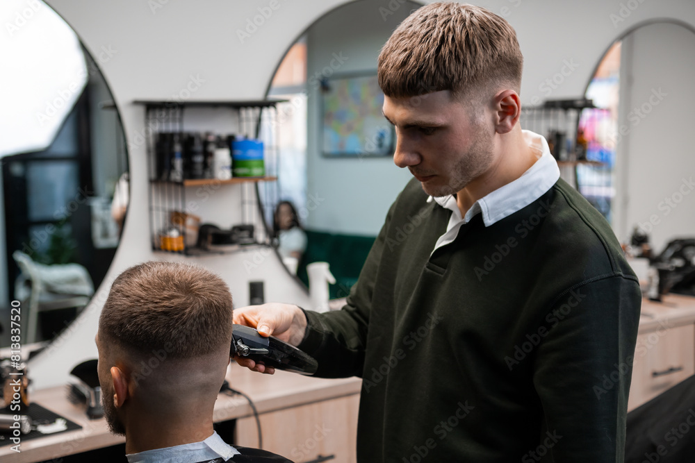 Barber uses shaver machine to cut young man hair in barbershop closeup ...