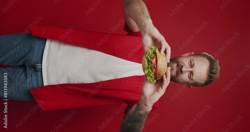 Vertical video of Unshaven caucasian man eats meat burger with pleasure ...
